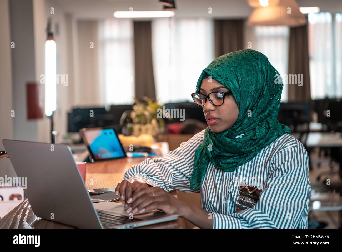Business woman wearing a green hijab using laptop in relaxation area at ...