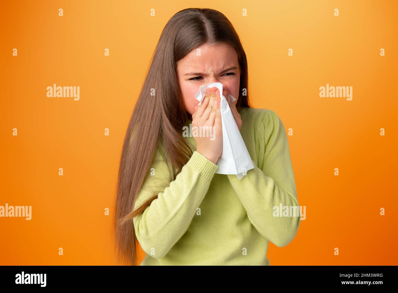 Teen girl blowing her nose against orange background Stock Photo - Alamy