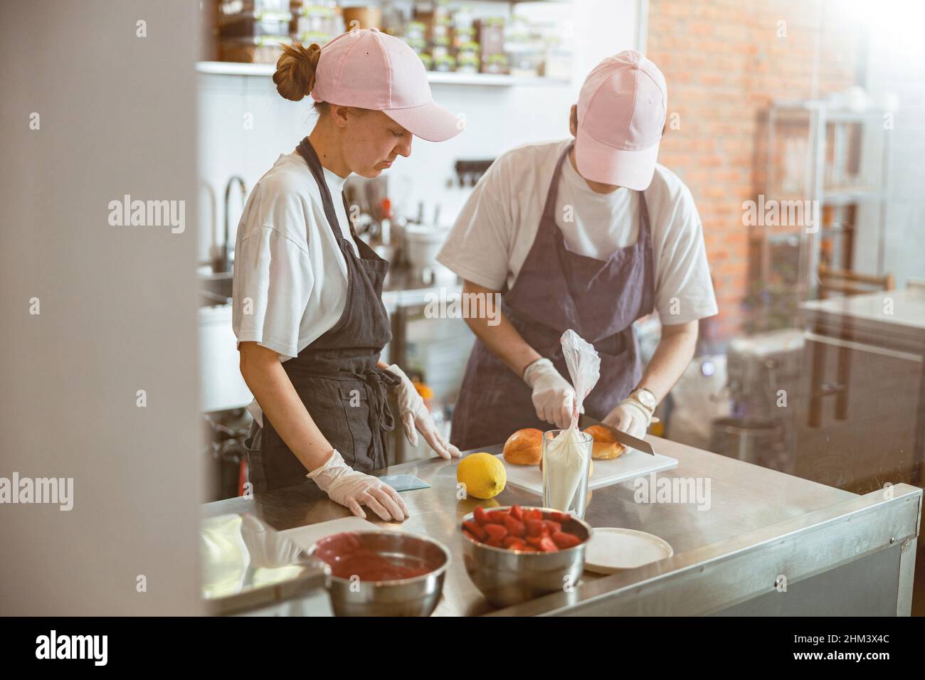 Young womancuts bun with colleague at metal counter in craft bakery ...