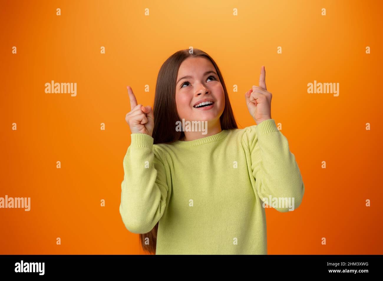 Cute teen girl pointing on copy space behing her back against orange ...