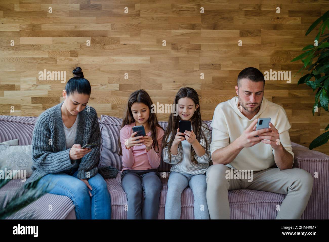 Family with two little daughters, everyone is using mobile phone in the ...