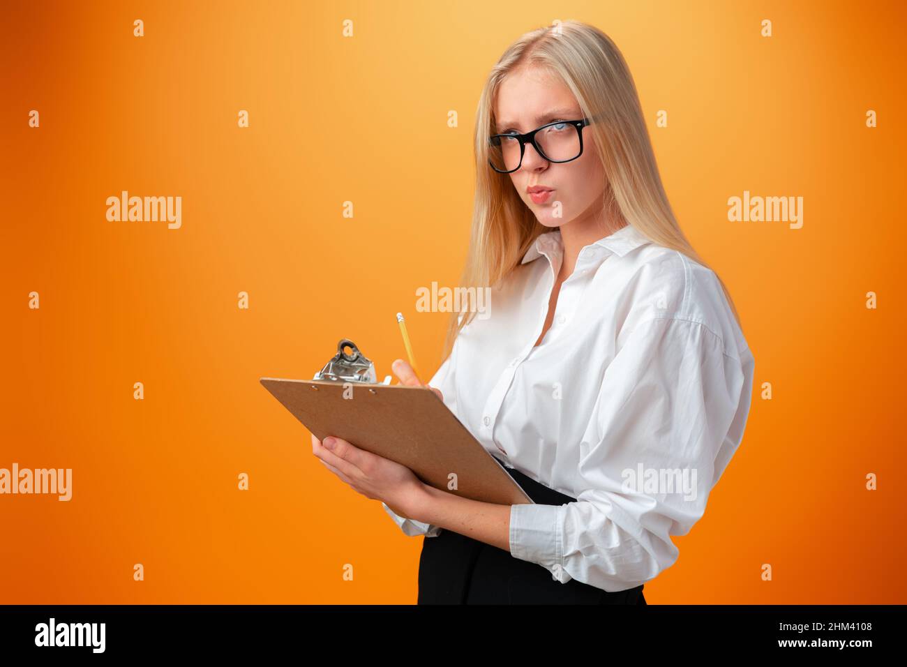 Teen school girl taking notes on clipboard against orange background ...