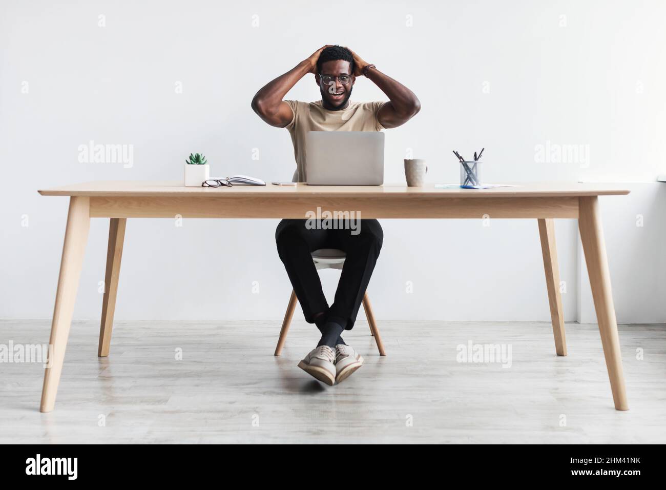 Shocked black man sitting at desk with laptop, grabbing head in terror ...