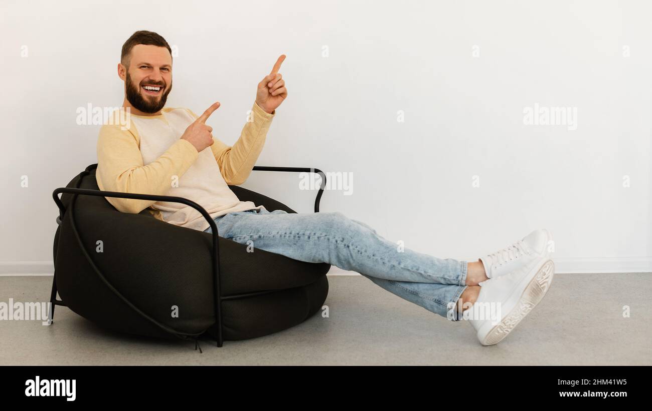 Happy Man Pointing Fingers Aside Sitting In Chair Indoor Stock Photo ...