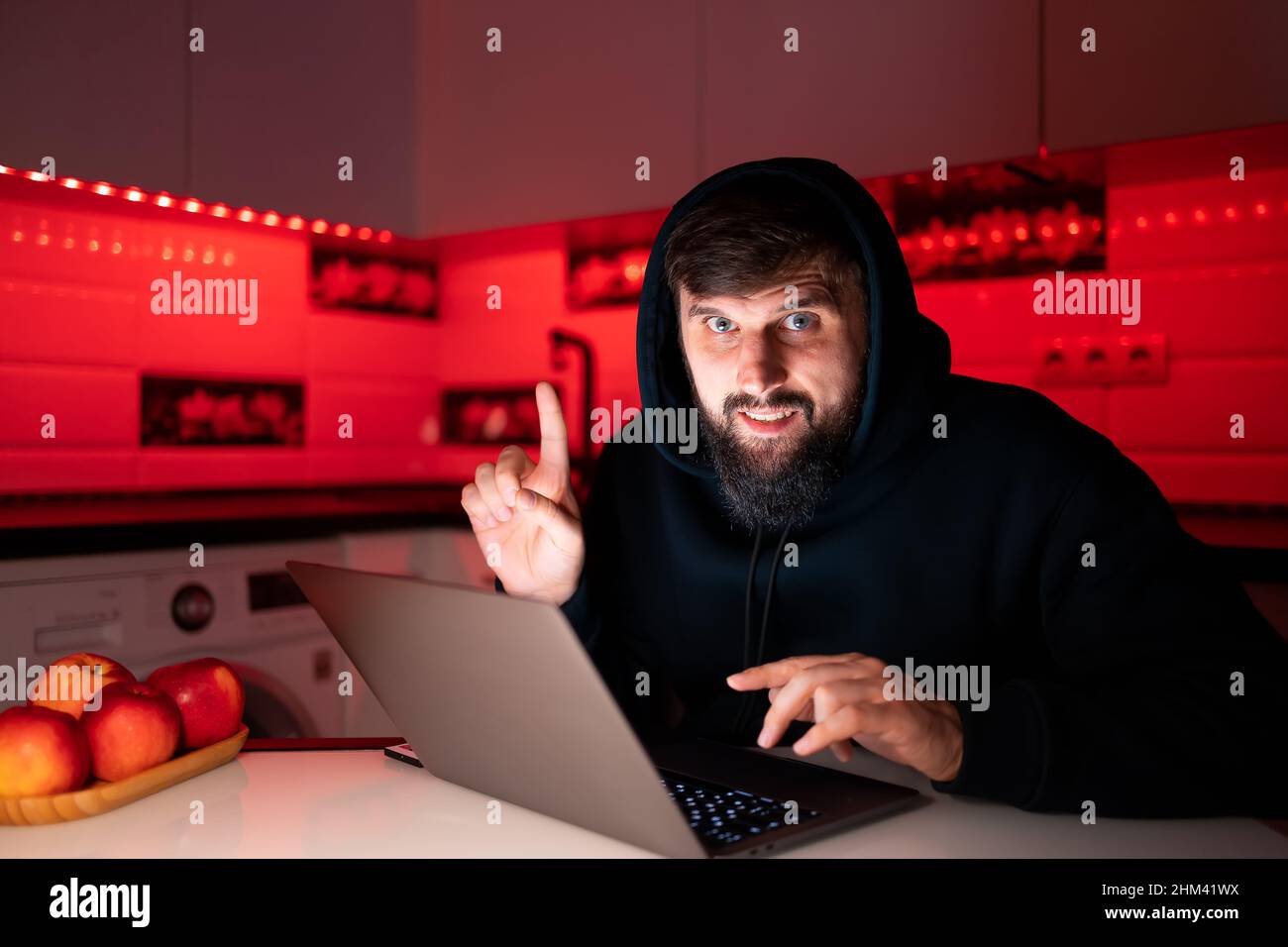 a male hacker behind a laptop in a dark room points his finger up Stock ...