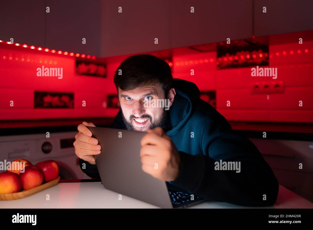 a male hacker behind a laptop in a dark room holds his hands on the ...