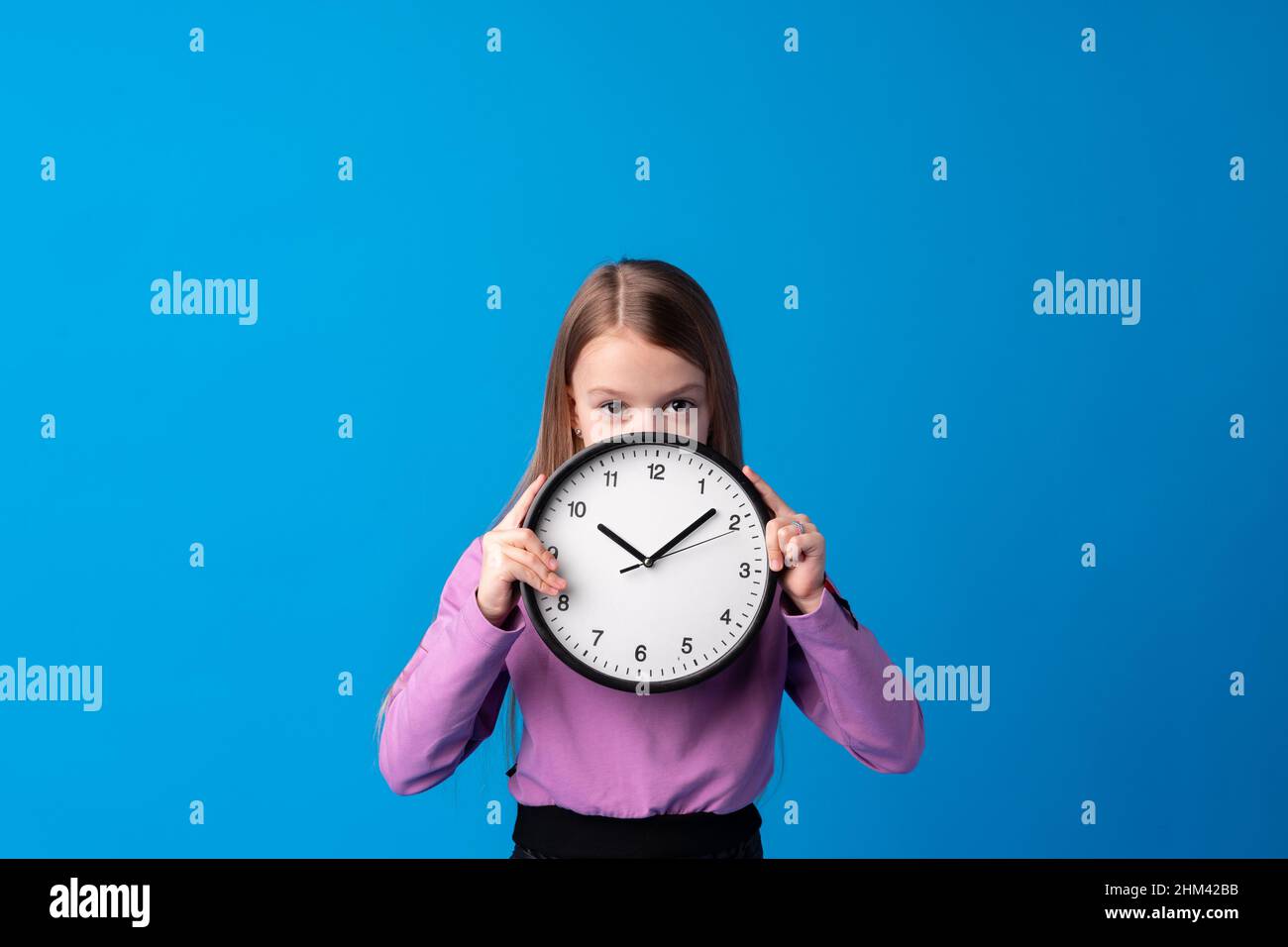 Beautiful teen girl holding wall clock over blue background Stock Photo ...