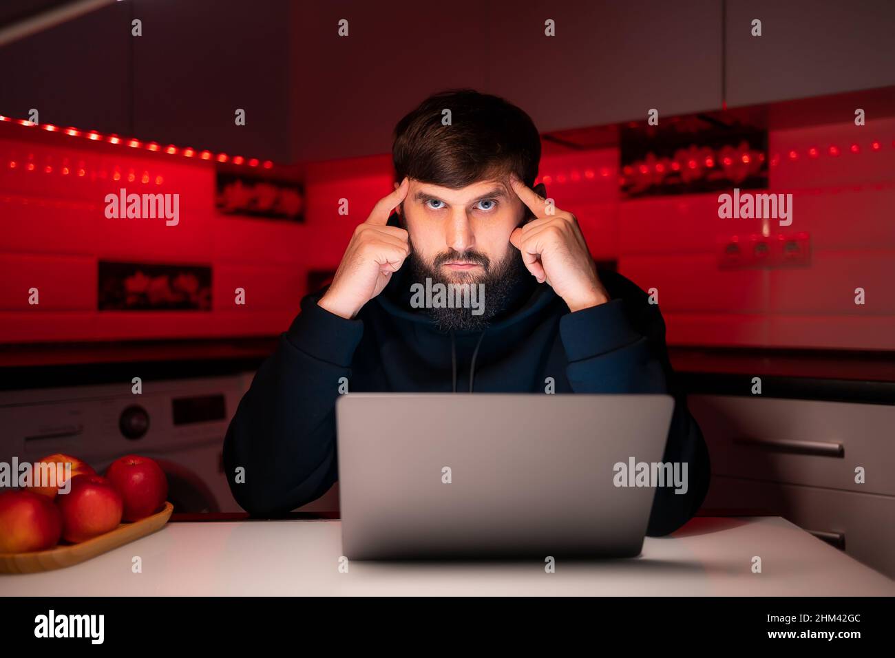 a hacker in a black hoodie is sitting at his laptop thinking Stock ...