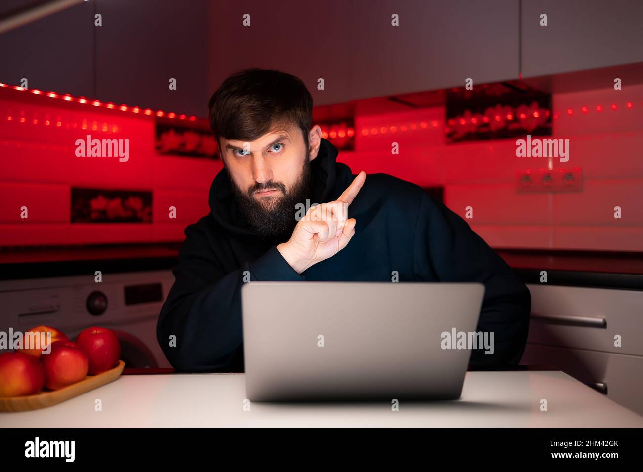 a hacker in a black hoodie is sitting at a laptop pointing his fingers ...