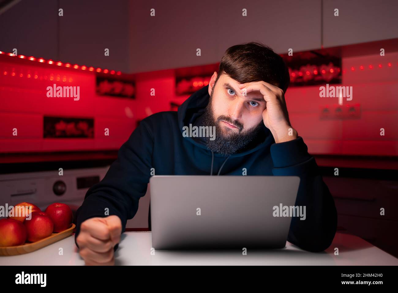 a hacker in a black hoodie is sitting at a laptop, showing his palms ...