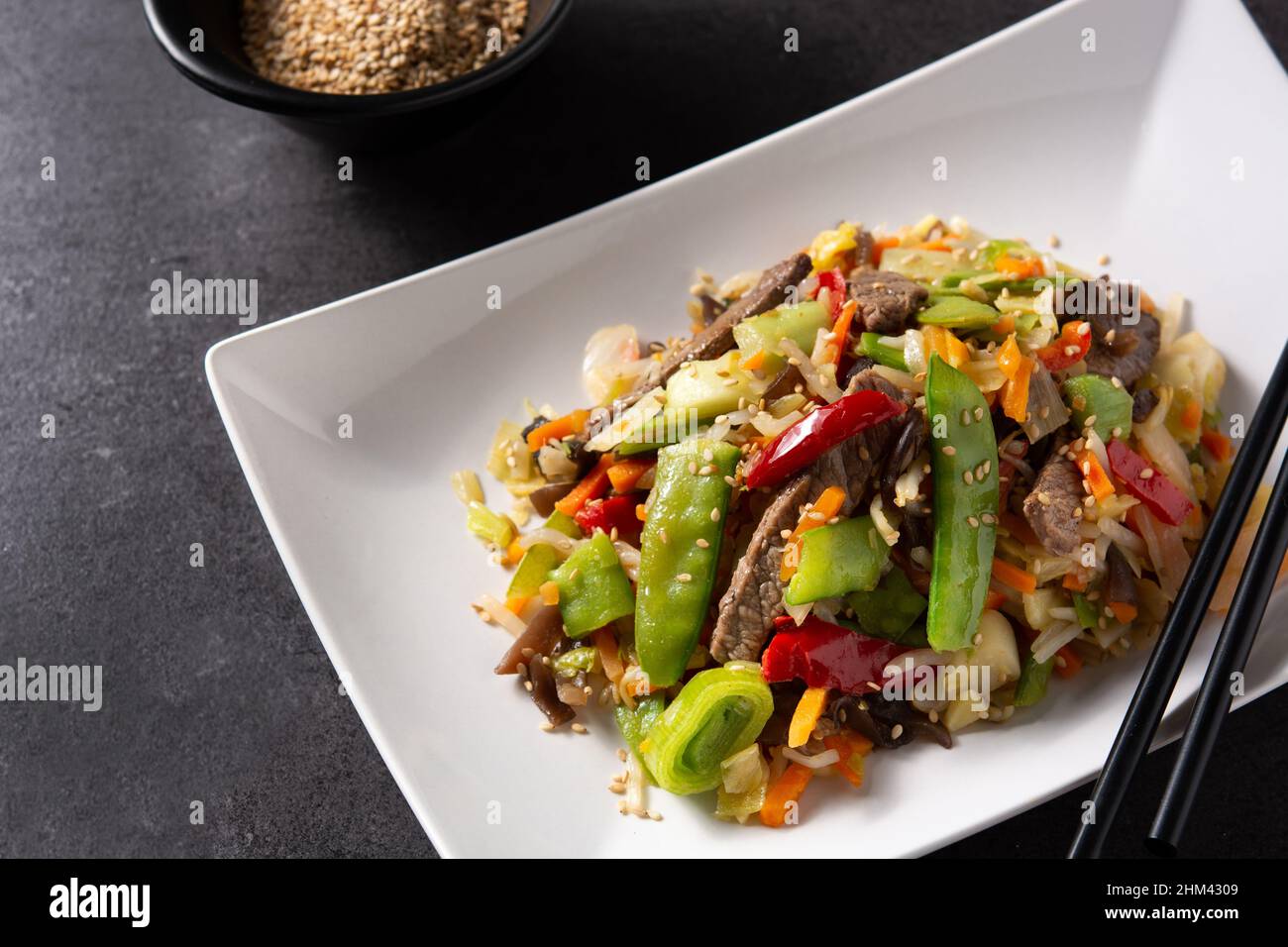 Beef, vegetables and sesame seeds in white plate on black background ...