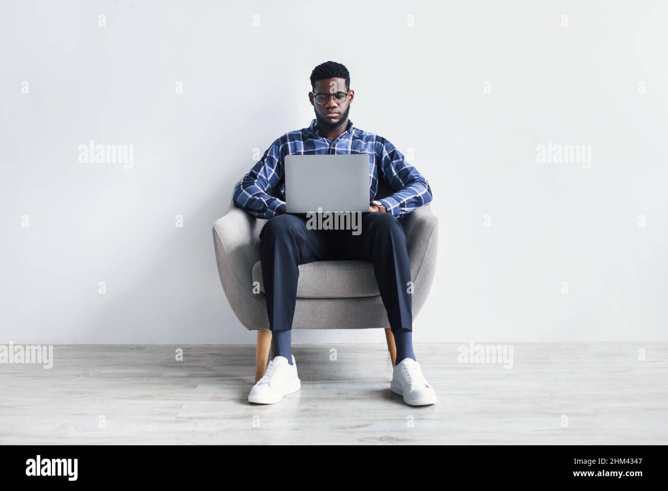 Full length of focused millennial black guy with laptop pc sitting in ...