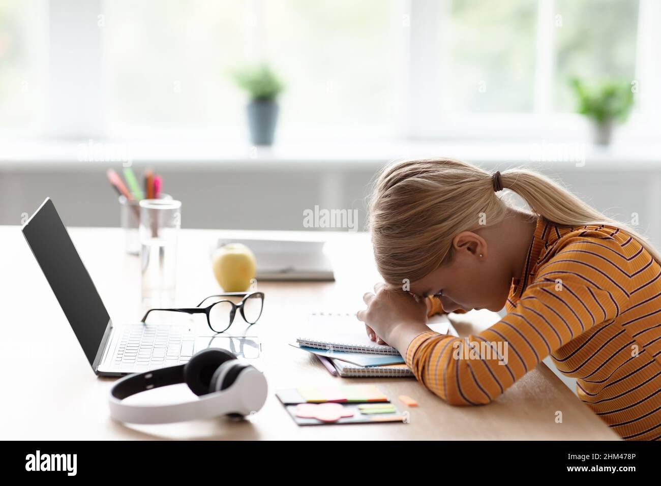 Sad tired caucasian teenage girl blonde put her head on table resting ...