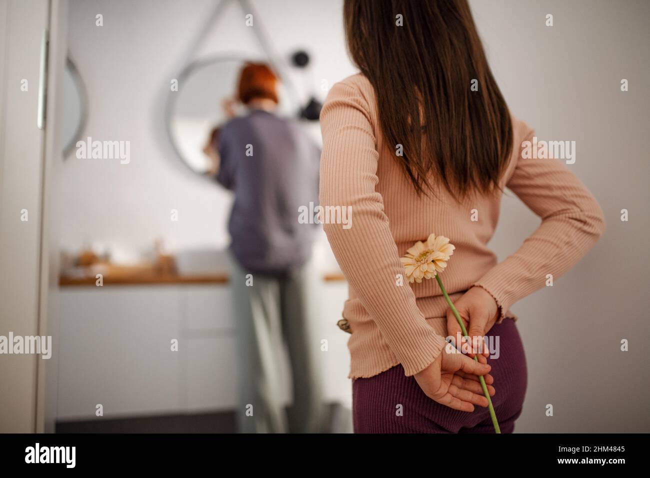 Close-up of little girl hiding flower and bringing it to her mother in ...