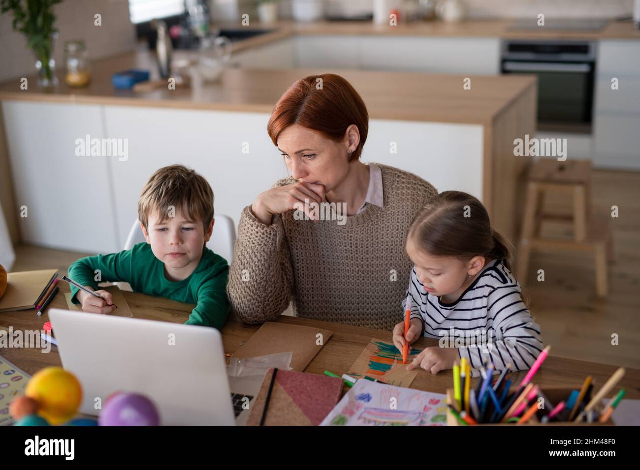 Mother of little children supervising them when distance learning and ...