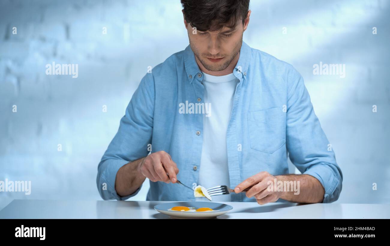 man with fork and knife eating fried eggs for breakfast Stock Photo - Alamy