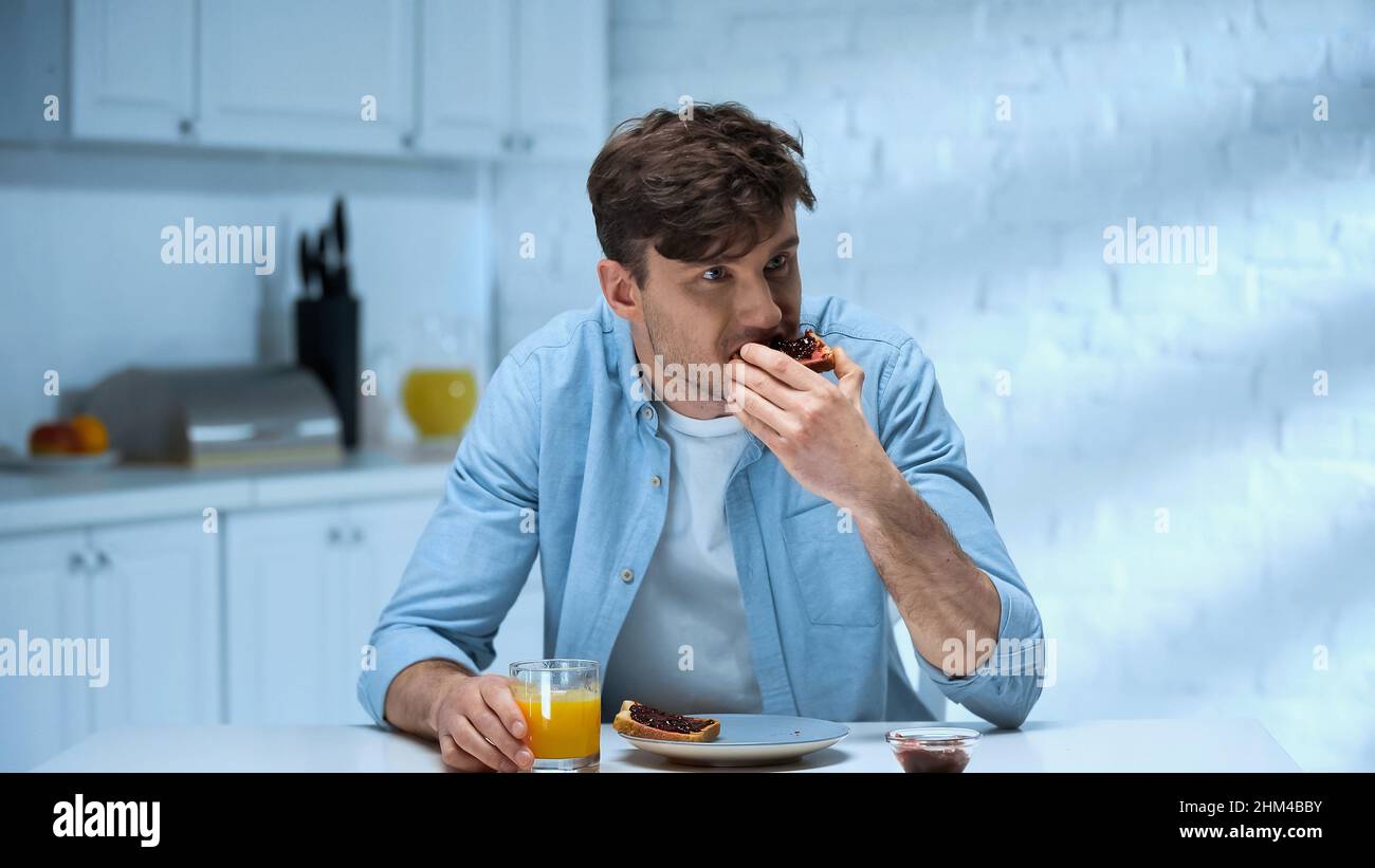 man eating toast with confiture near glass of orange juice in kitchen ...