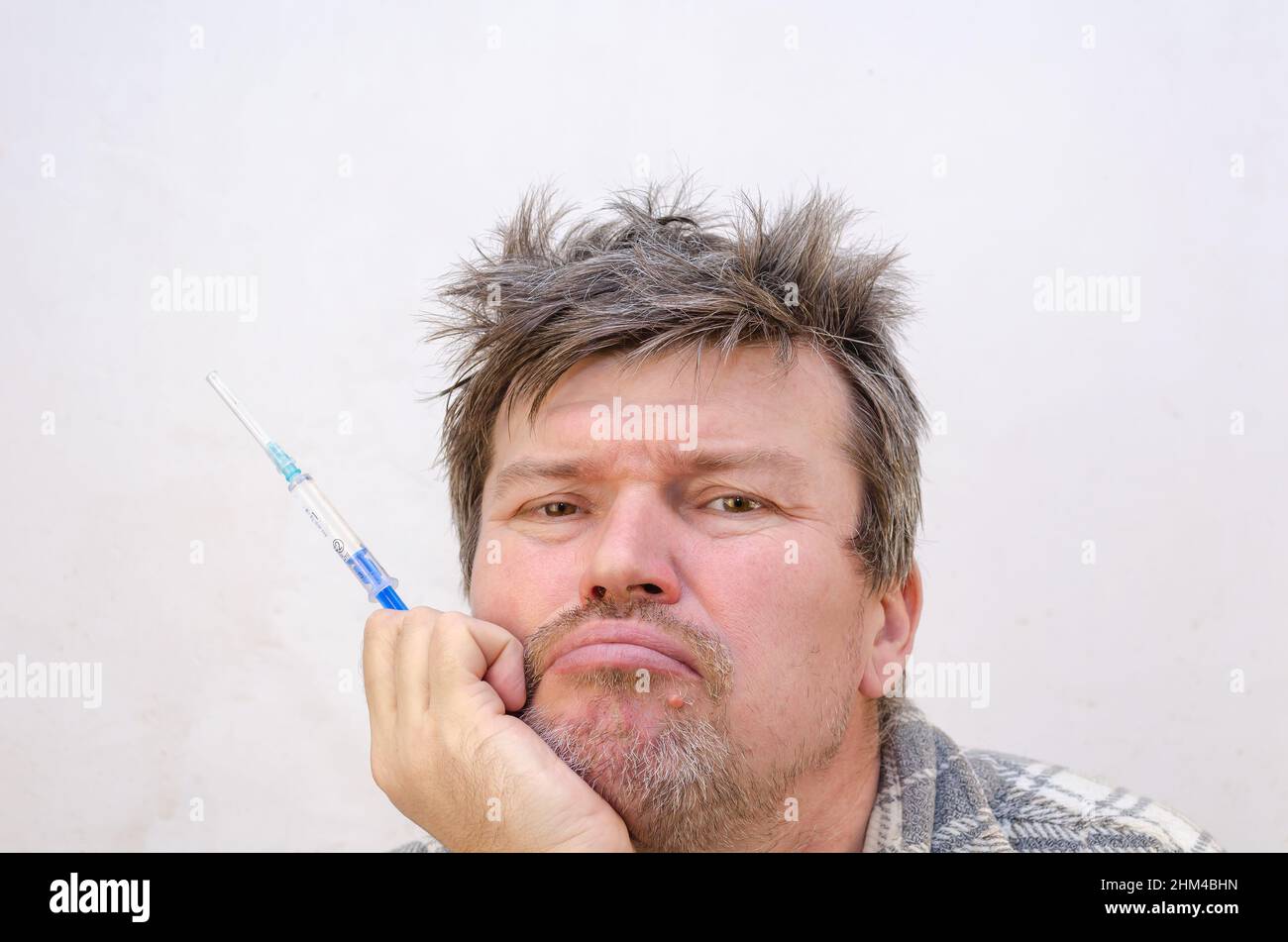 Portrait of a brooding adult male with a blue syringe. Annoyed male ...