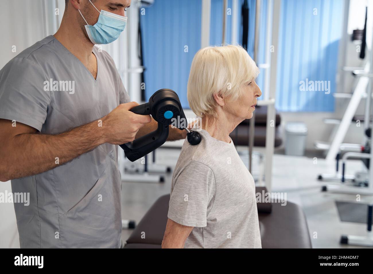 Medical worker giving massage to elderly woman with percussion massager ...