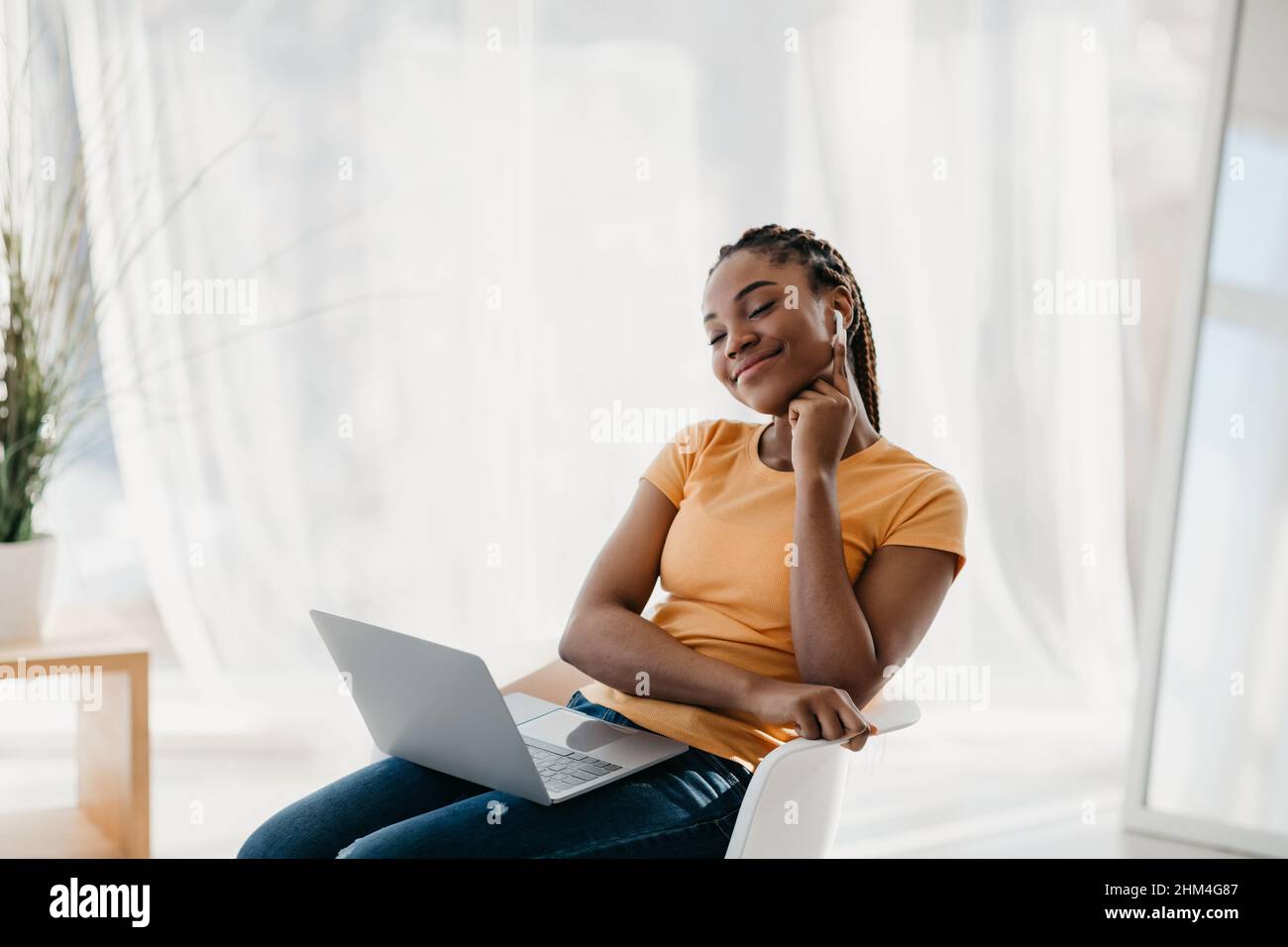 Young black woman using laptop computer, wearing earphones, relaxing ...