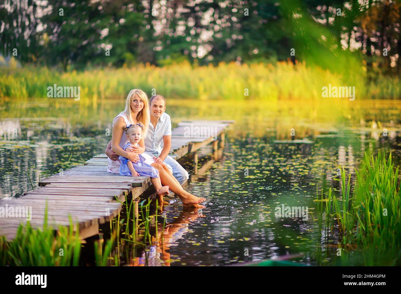 happy family resting sitting on a wooden pier, dip their feet in the ...