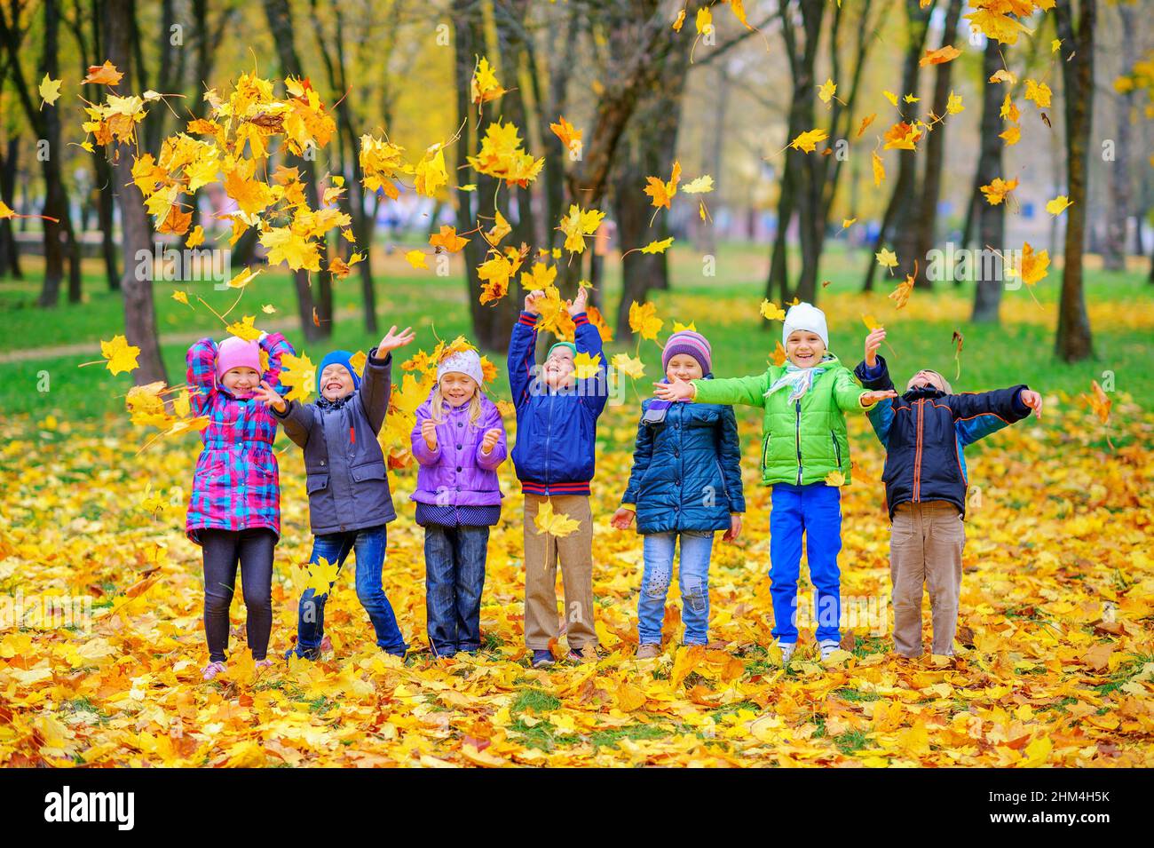 group of children playing in the autumn park, tossing up autumn foliage ...