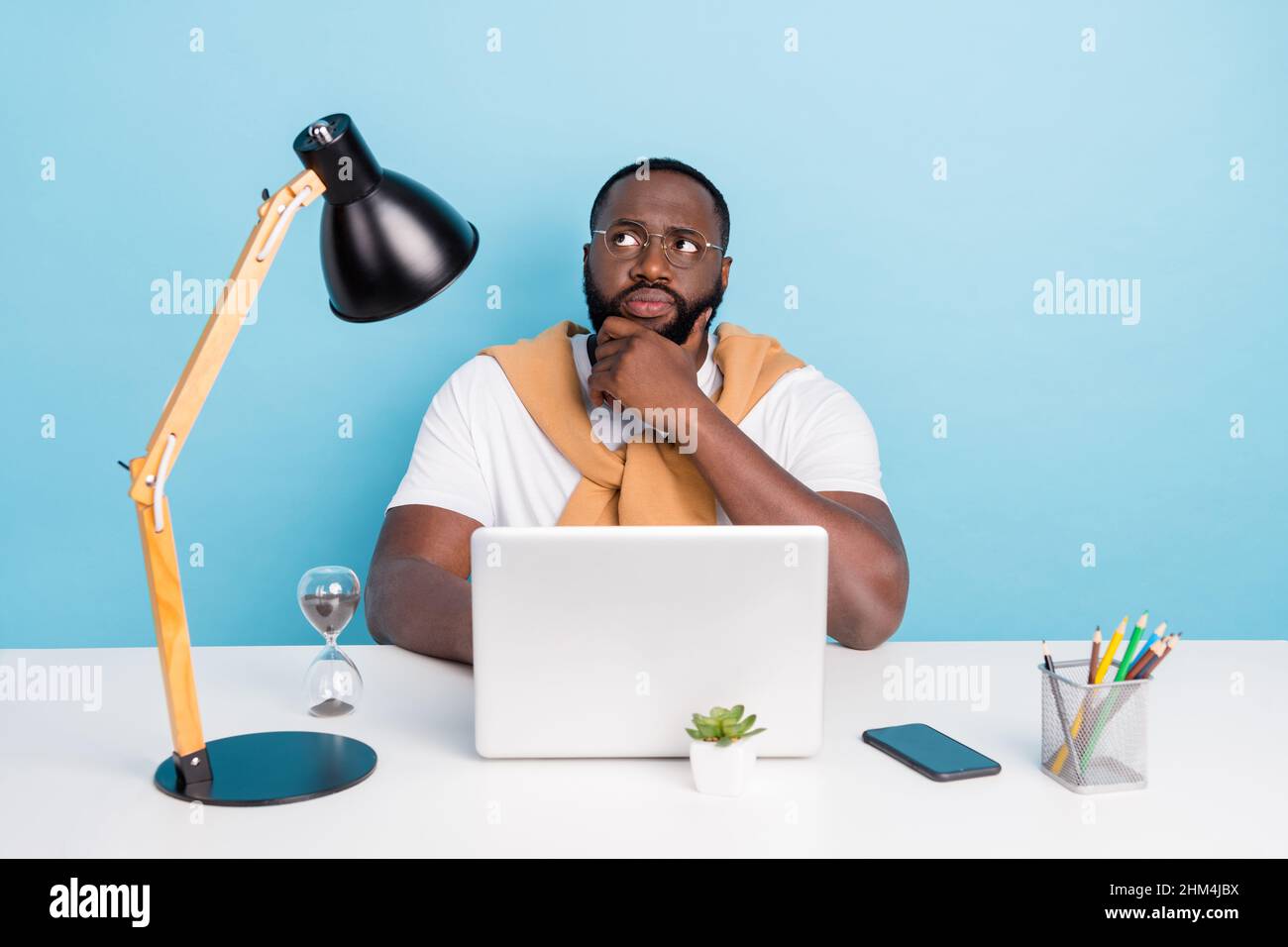 Photo of minded guy sit table pc look empty space decide wear white t ...