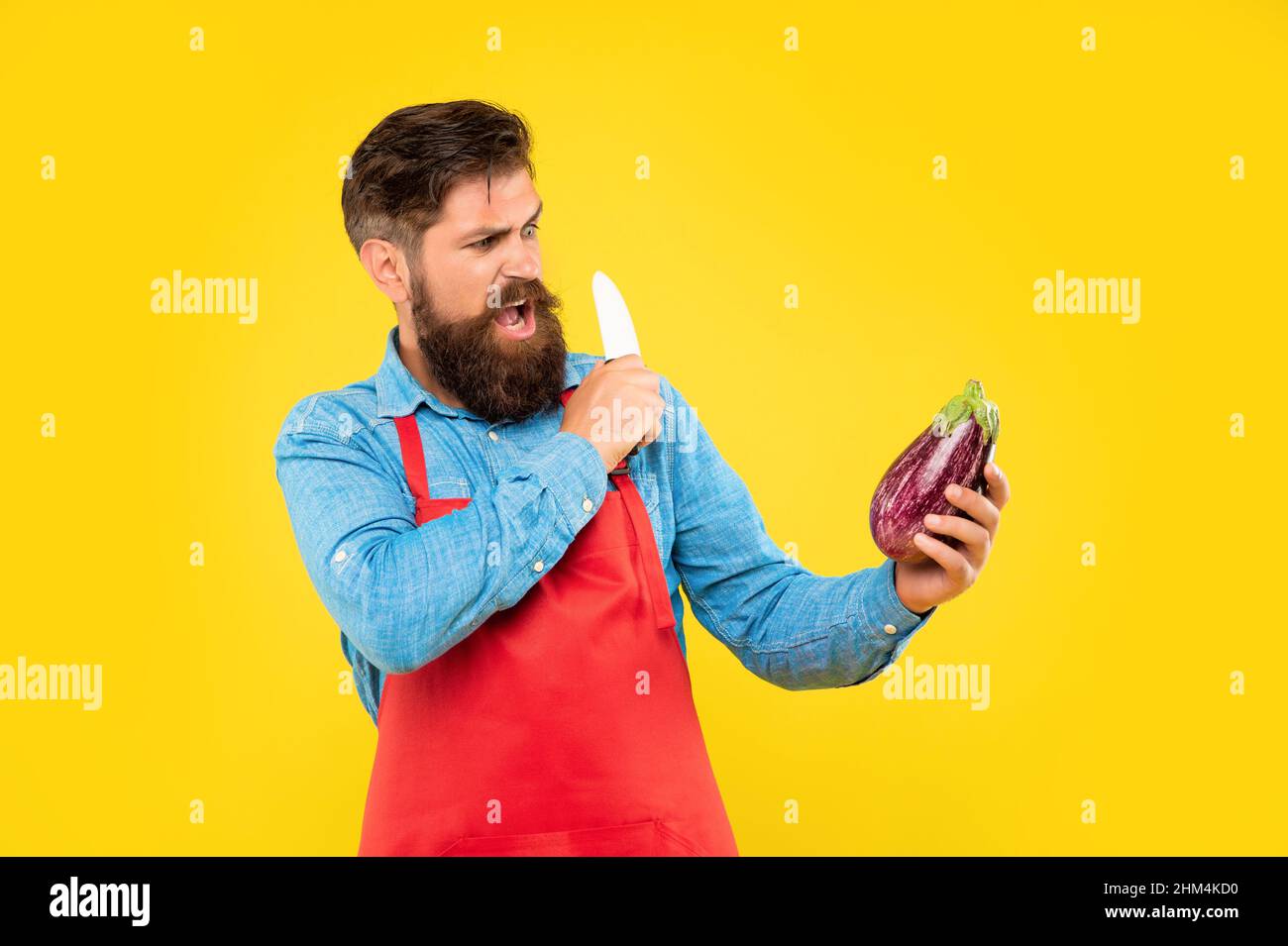 Angry man in apron holding cooks knife and eggplant yellow background ...