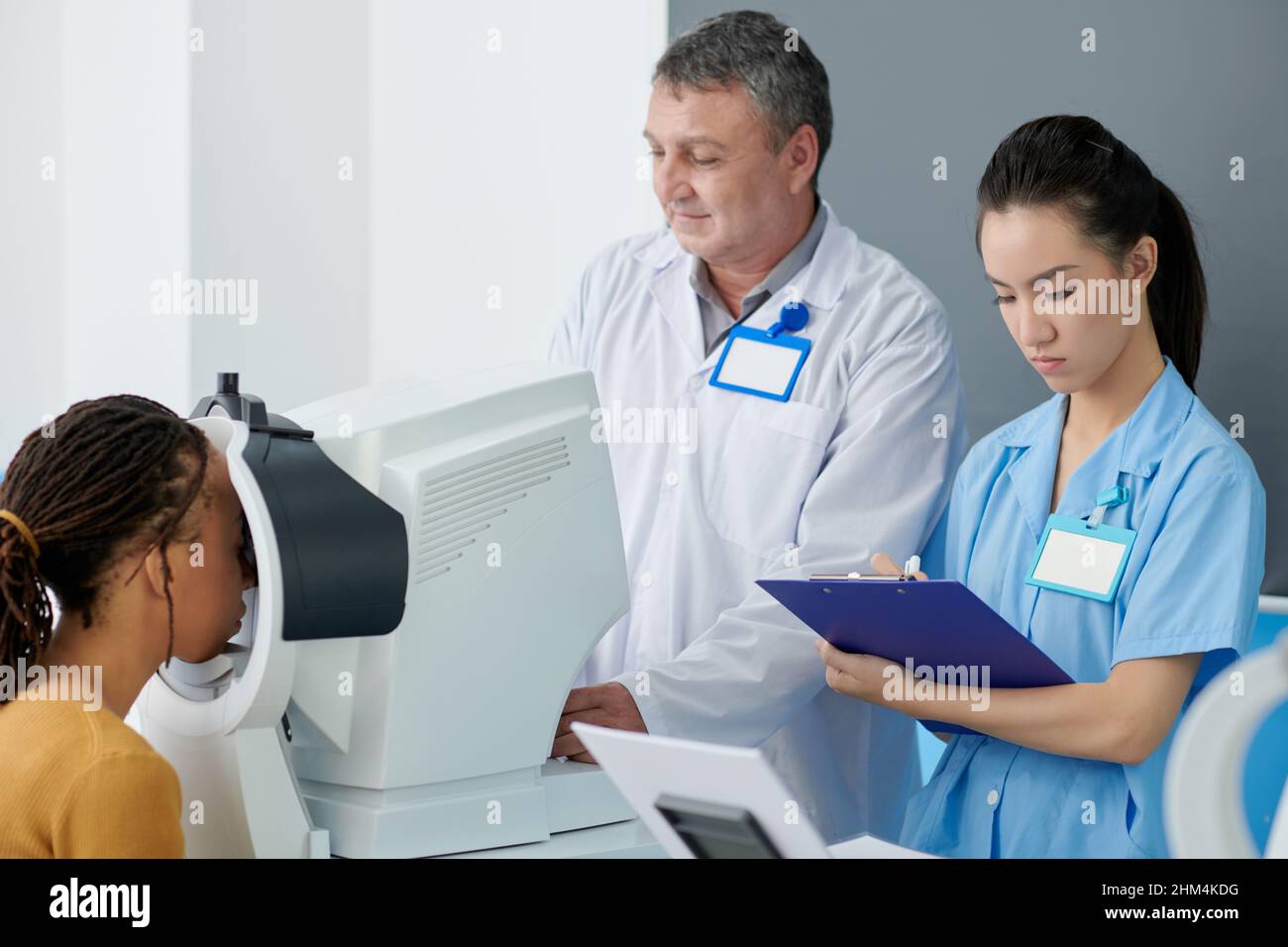 Medical nurse taking notes in document when doctor examining eyes of ...