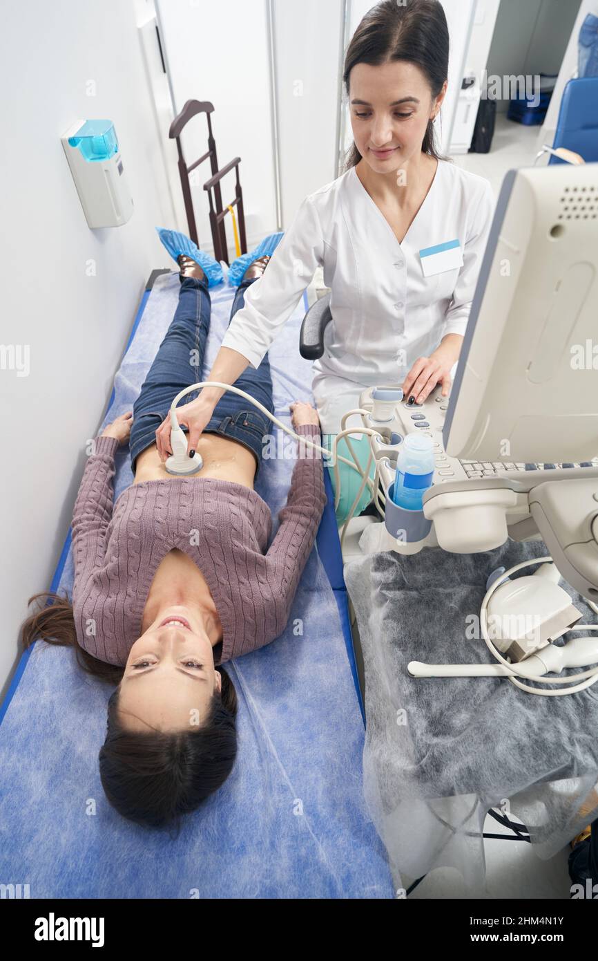 Focused doctor moving ultrasonic transducer over abdomen of young woman ...