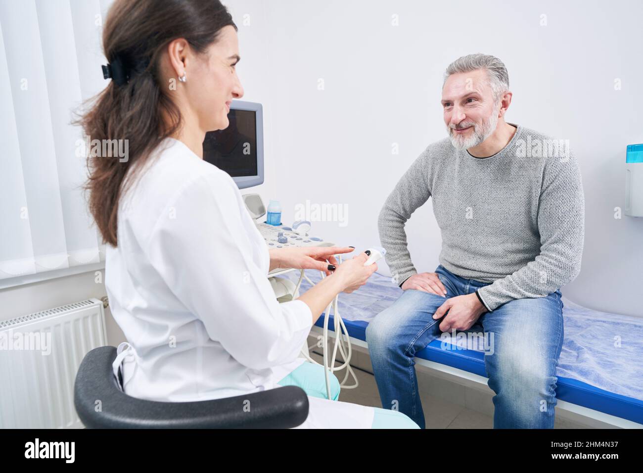 Friendly young sonographer communicating with patient before ...
