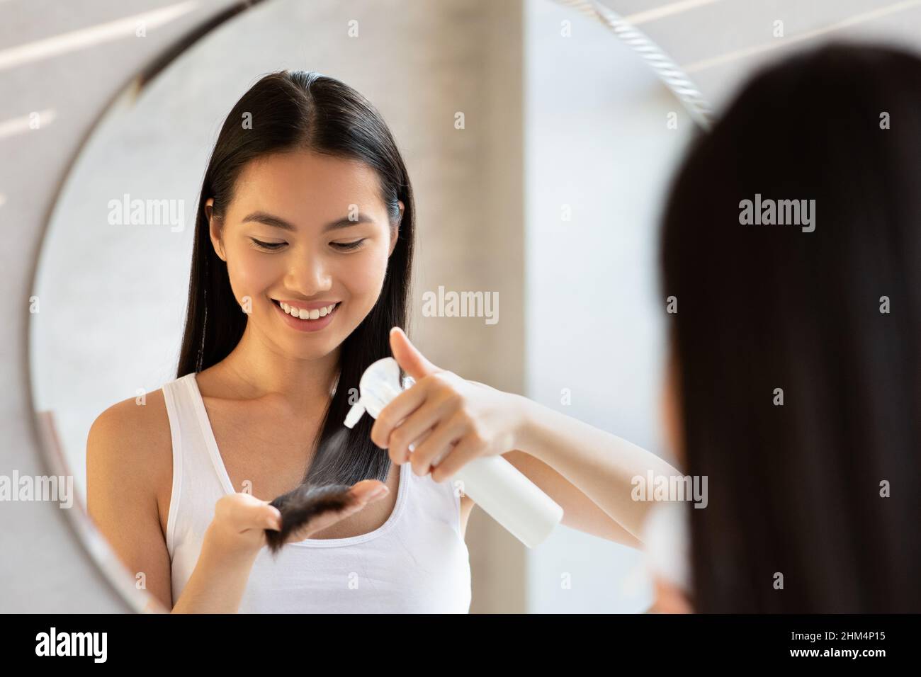 Happy long-haired young korean woman using hair spray Stock Photo - Alamy