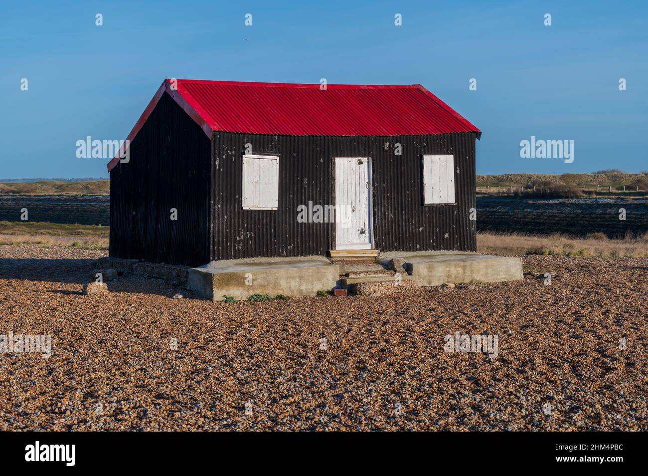 Red roofed hut at Rye Harbour, Sussex, UK, in early morning winter ...