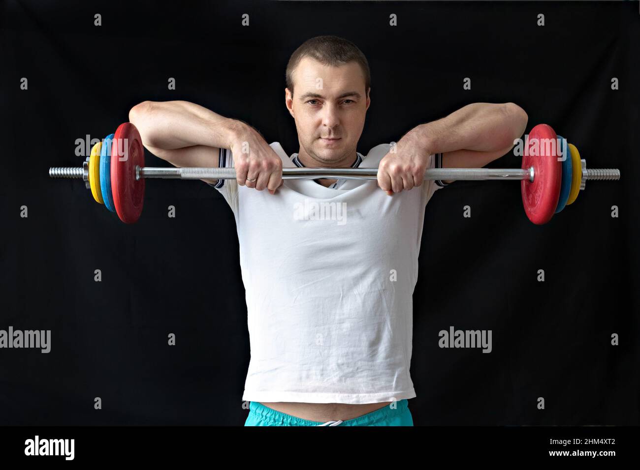 A strong, healthy man with muscles, training at home with a barbell ...