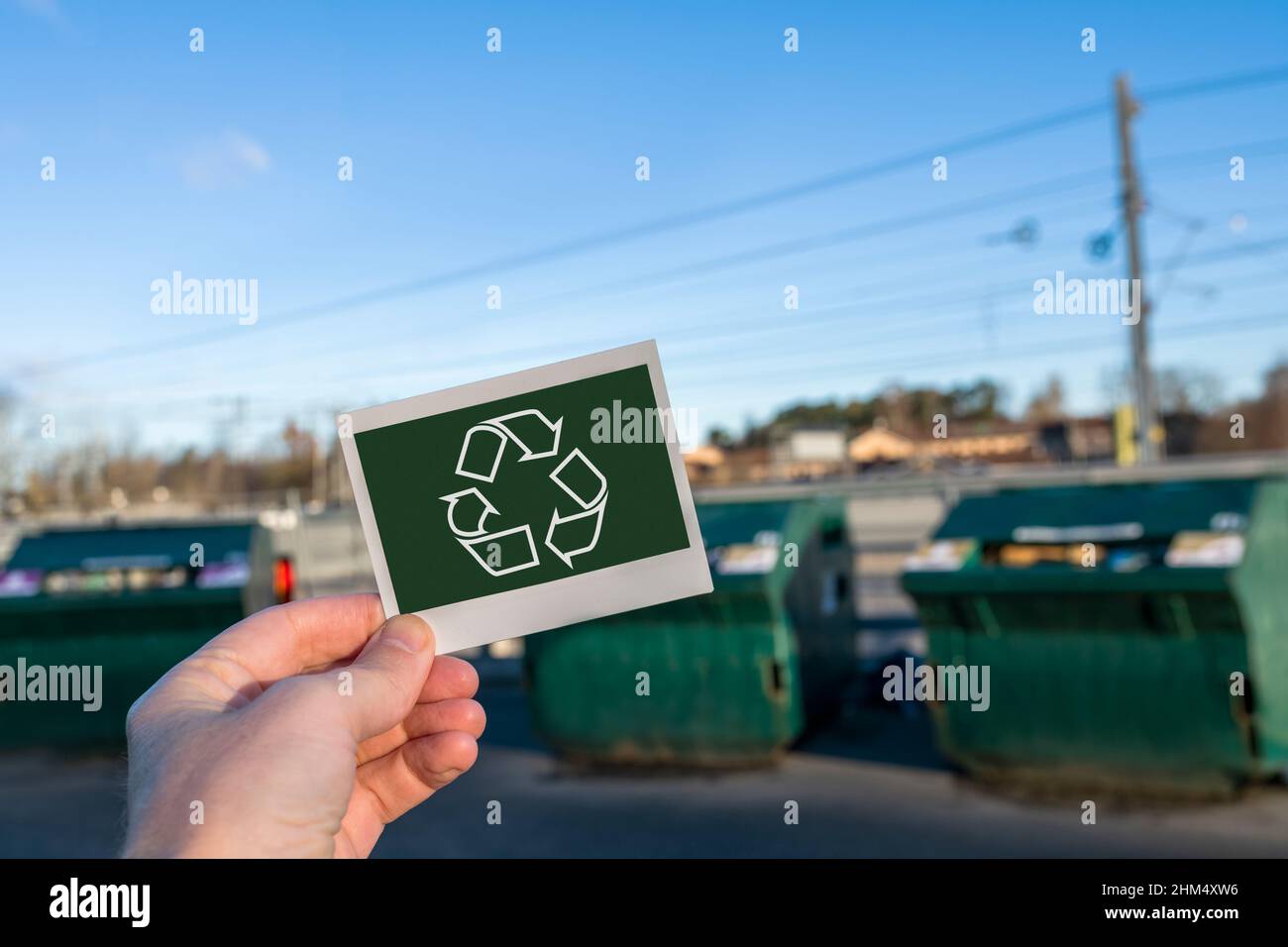 Hand holding recycling sign in front of bins Stock Photo - Alamy
