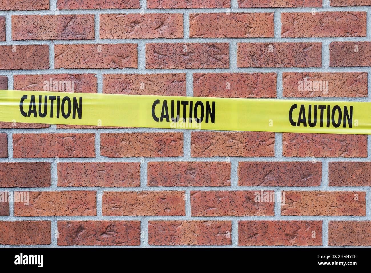 Caution yellow tape closeup against red brick wall Stock Photo - Alamy