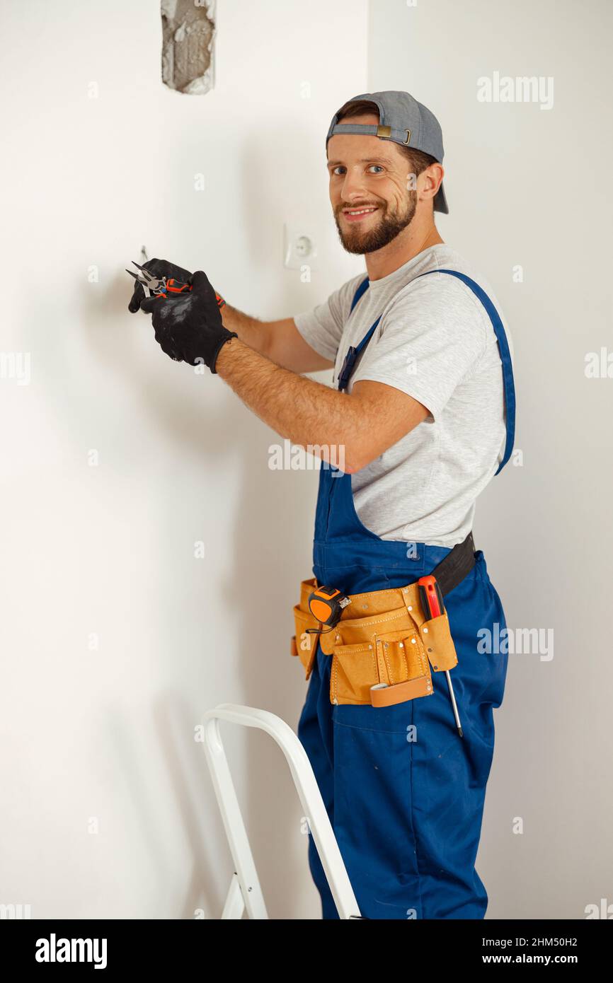 Happy handyman electrician smiling at camera, holding pliers while ...