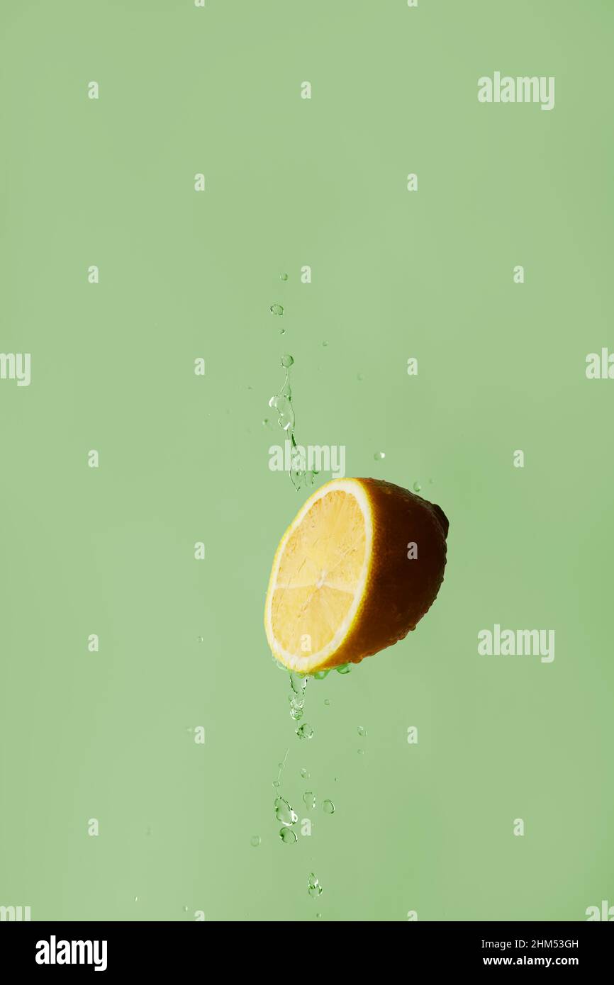 A cut juicy half of a lemon with splashes of water on a green ...