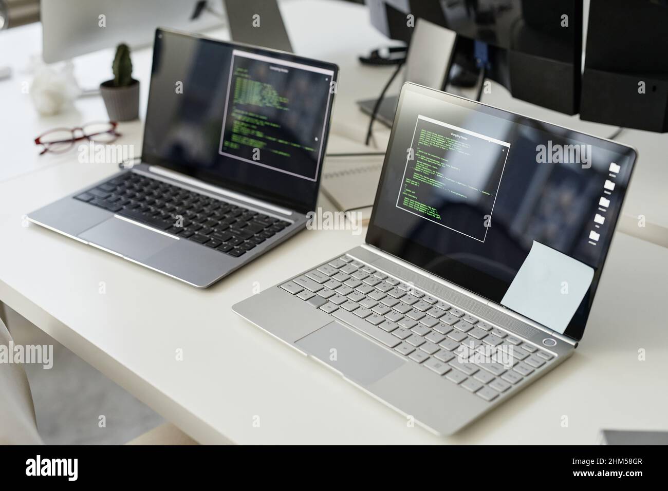 Two laptop computers with coded data and notepapers on screens standing ...