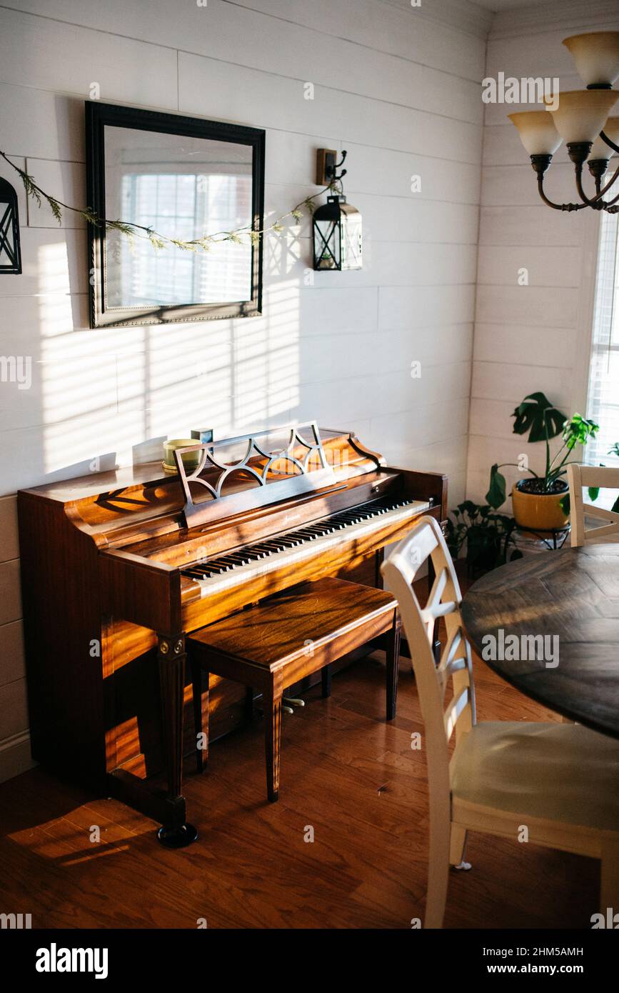 Piano in dining room with window light, shiplap walls, and table Stock ...