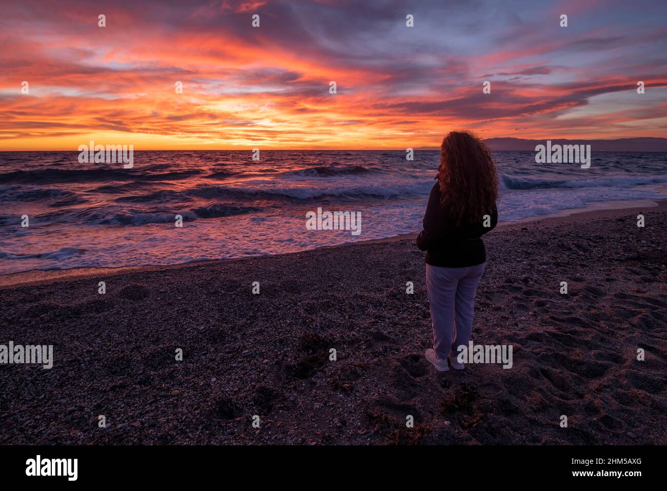 Woman on beach watching sunset Stock Photo - Alamy