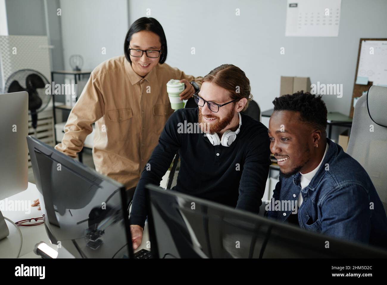 Three cheerful young intercultural diversity programmers decoding data on computer screen at ...