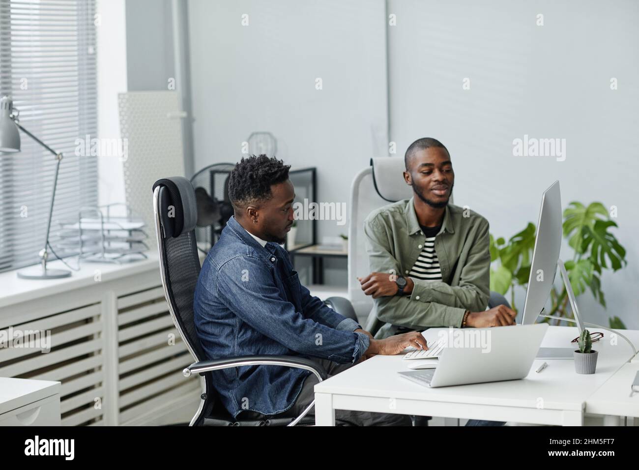 Two young confident programmers of African ethnicity sitting by desk in ...