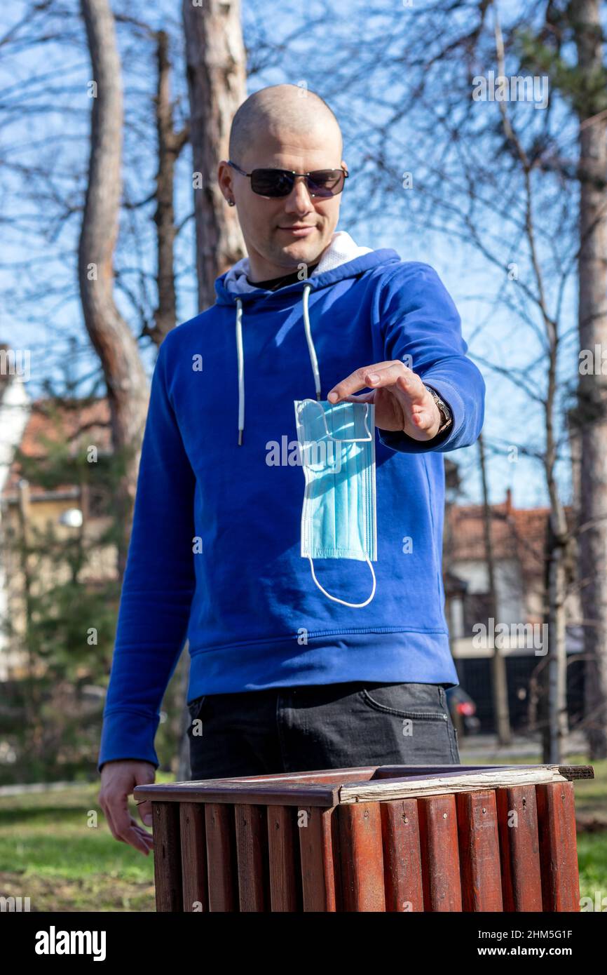 A young man in the park throwing away a protective face mask into the ...