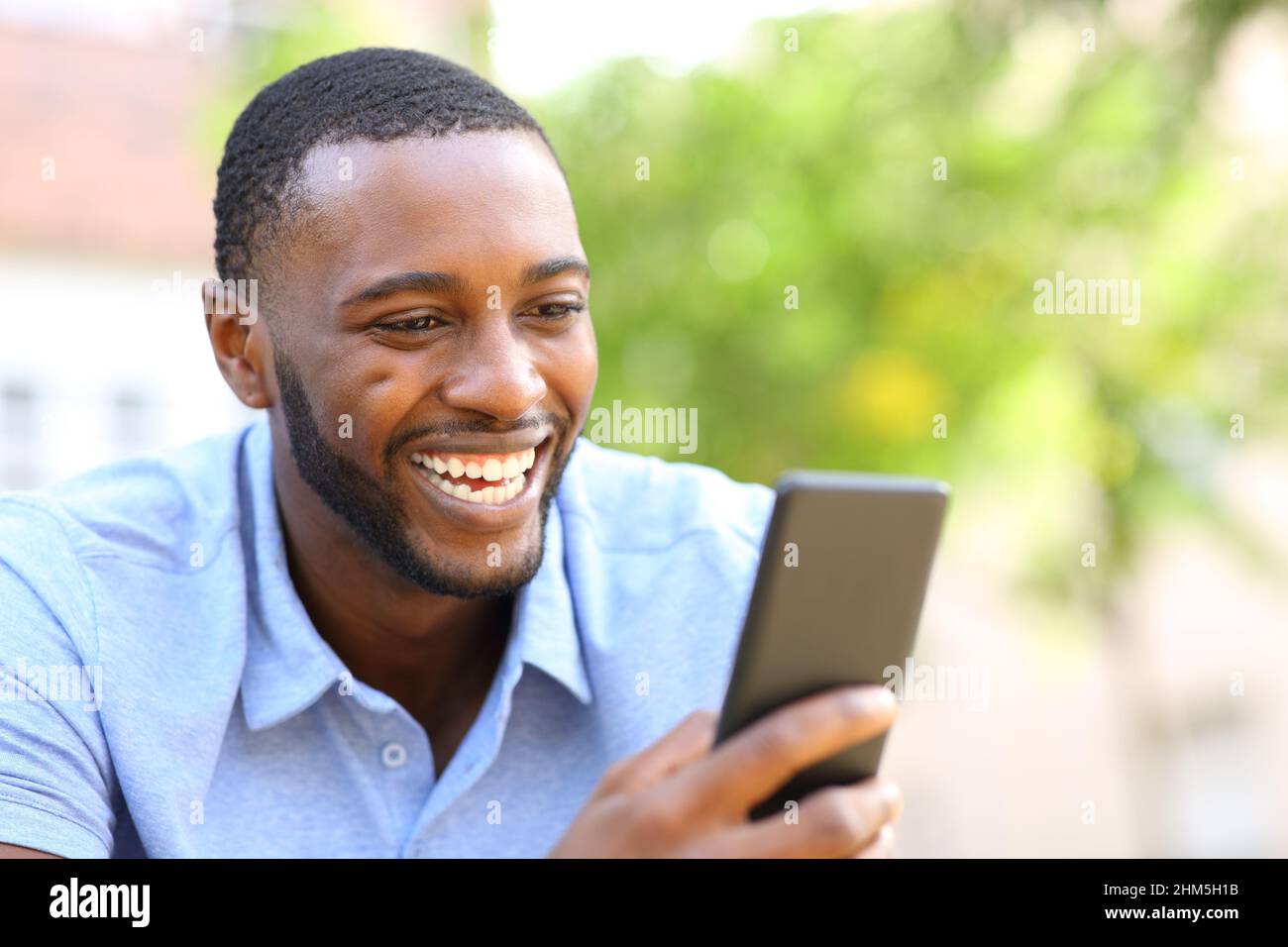 Happy man with black skin checking smart phone laughing sitting in a ...