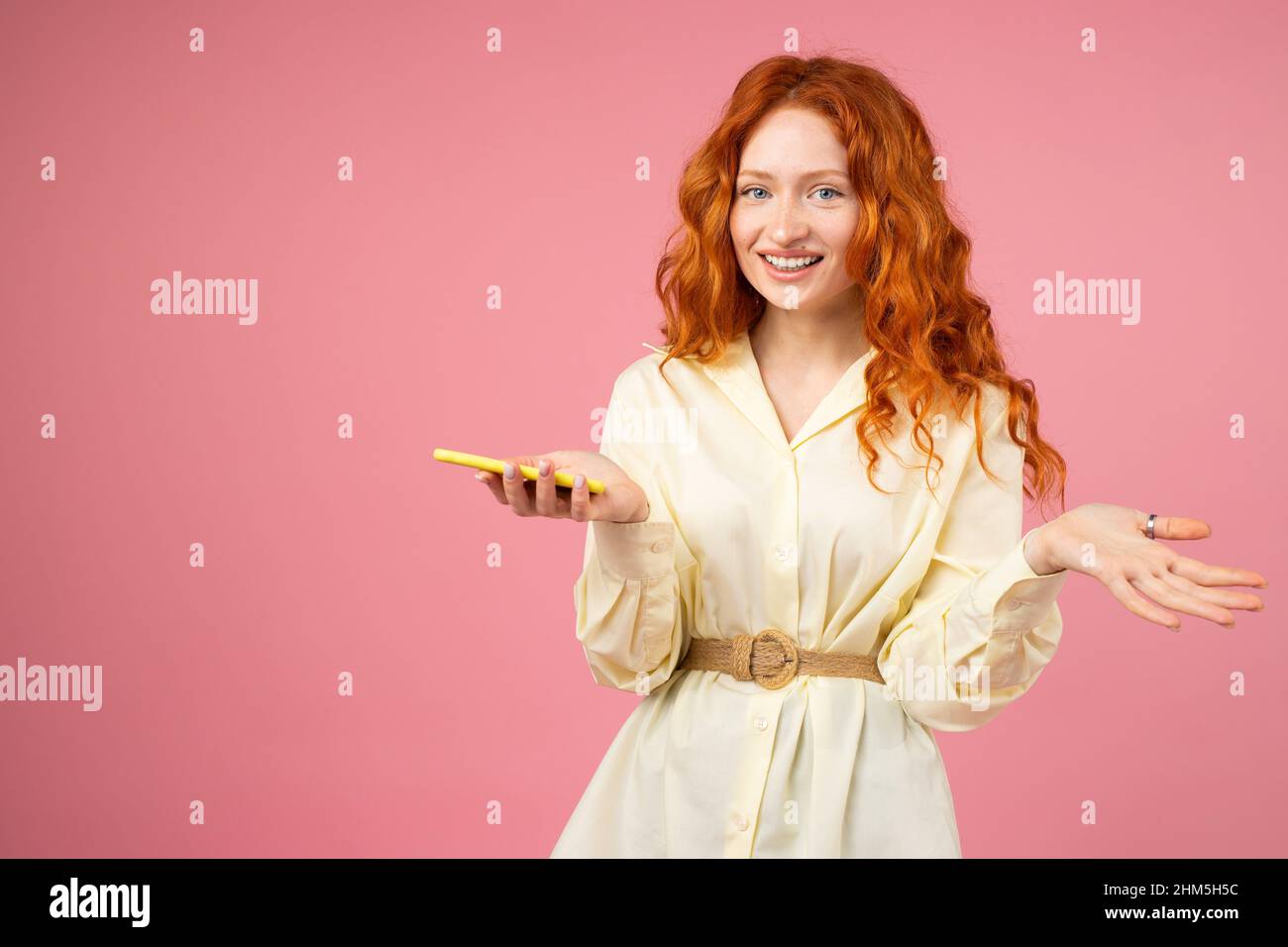 Young amazing redhead woman keeping smartphone in one hand and smiling ...