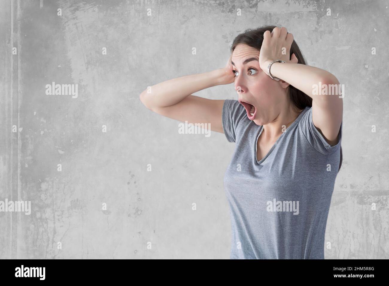 Angry woman screaming with her hands on head on a concrete background ...