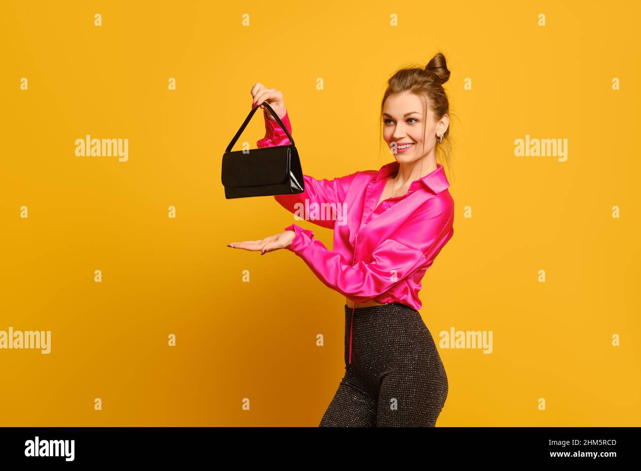 Happy woman stands in profile and holds her purse at arm against yellow ...