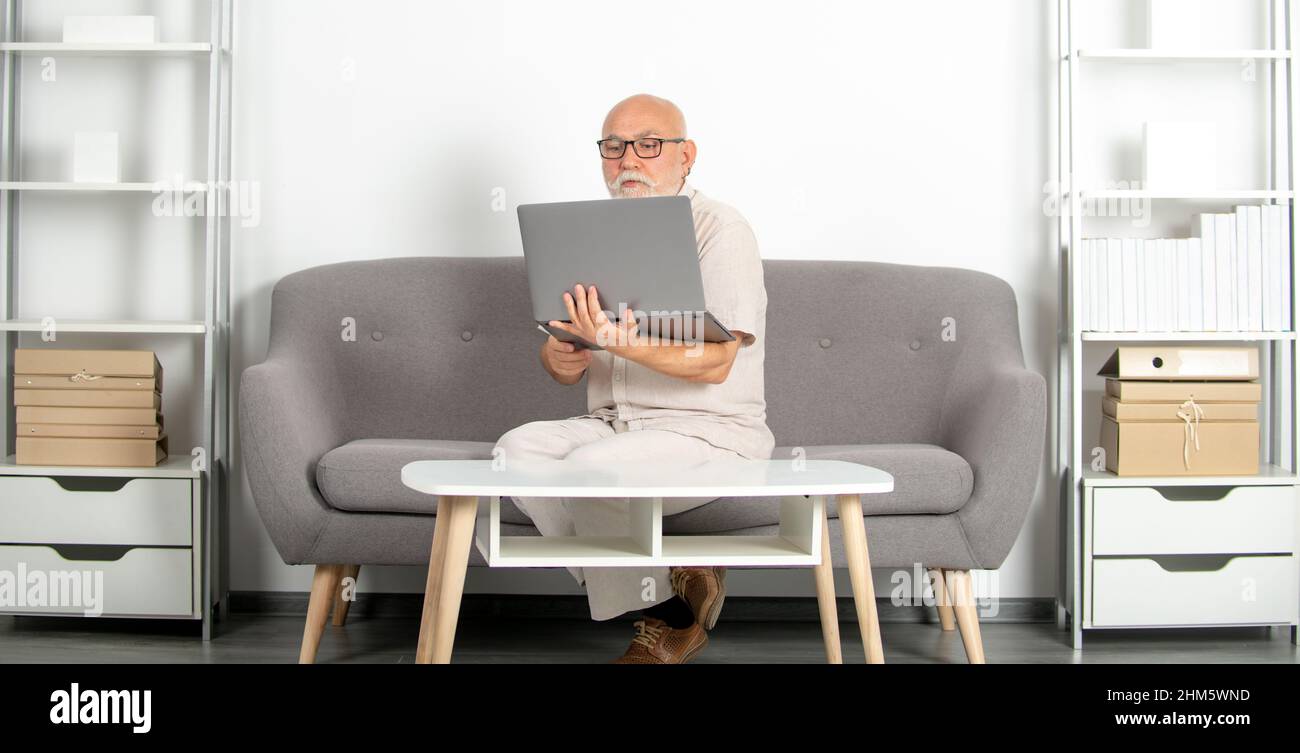 Mature consultant, senior man in office. Old man sits at desk on sofa ...