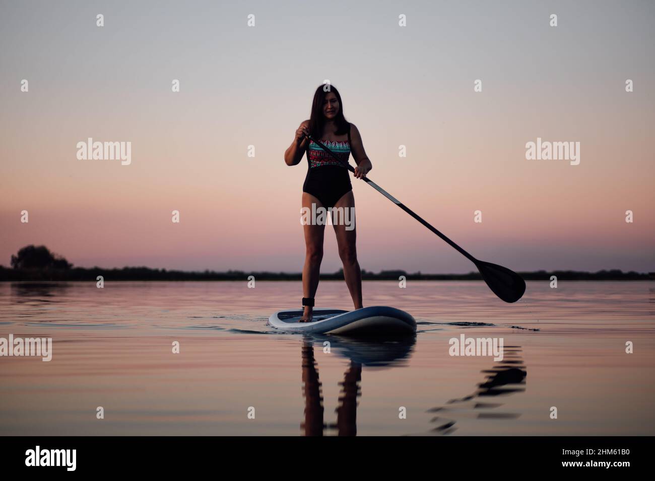Female sup boarder holding oar in hands rowing looking at camera on ...